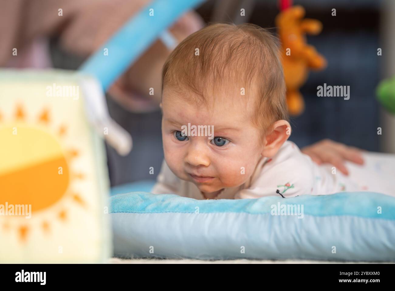 Baby exploring a colorful playmat with curious blue eyes and light ...