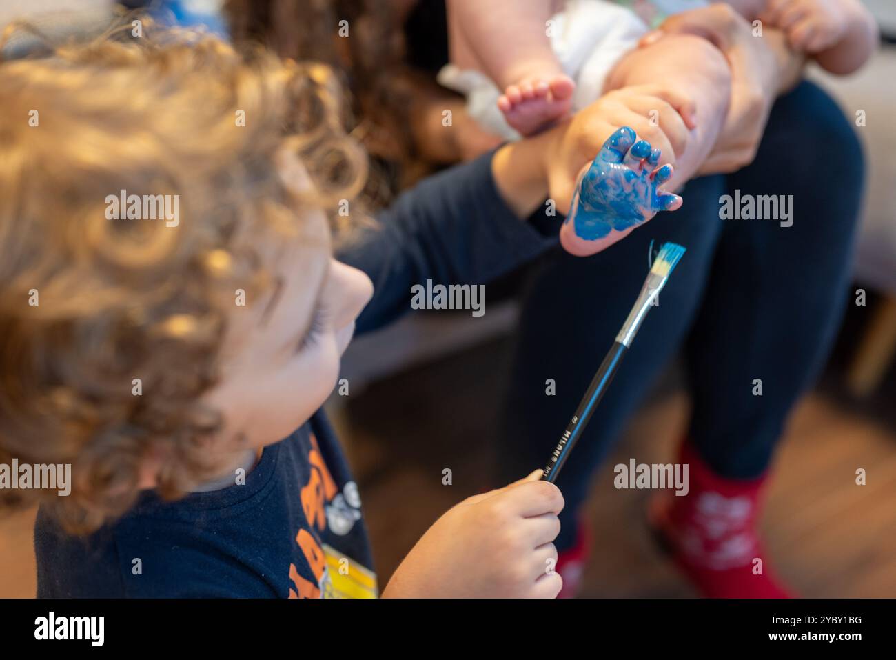 Little boy painting his baby sisters foot blue to make a footprint for ...