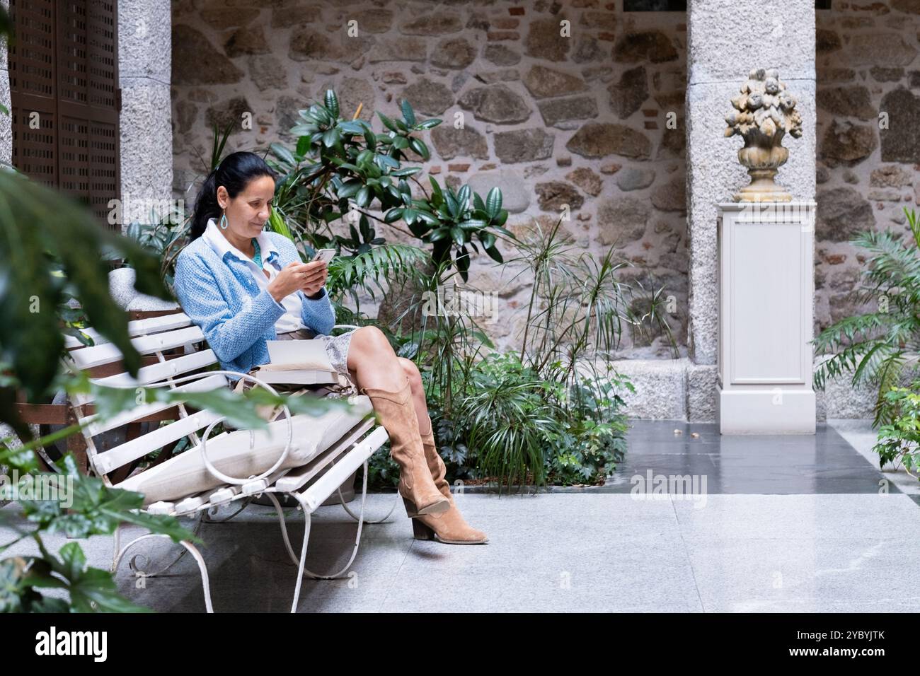 Side view of a beautiful adult woman scrolls on her phone sitting on a ...