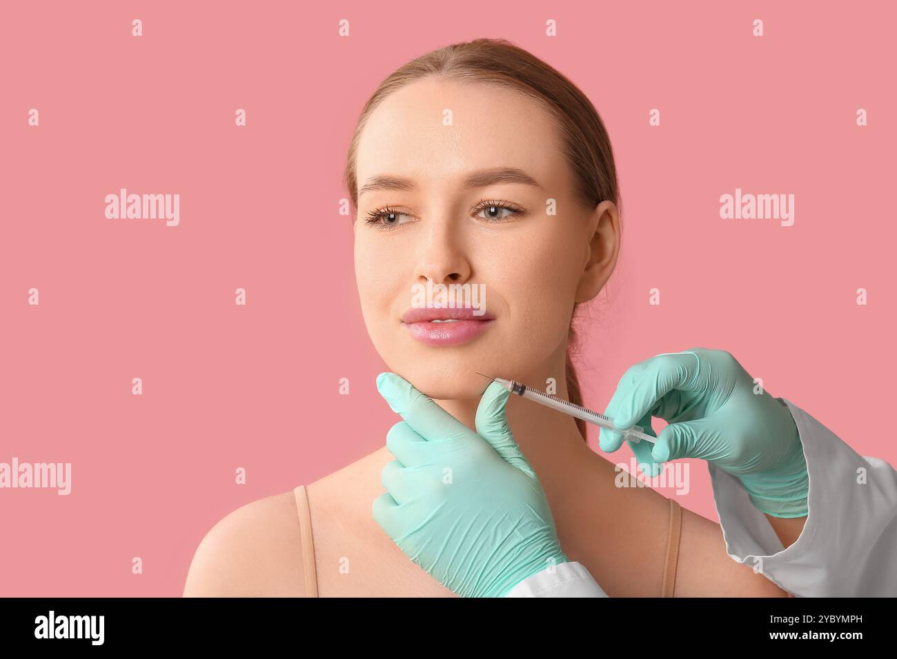 Beautiful young woman receiving filler injection in chin on pink ...