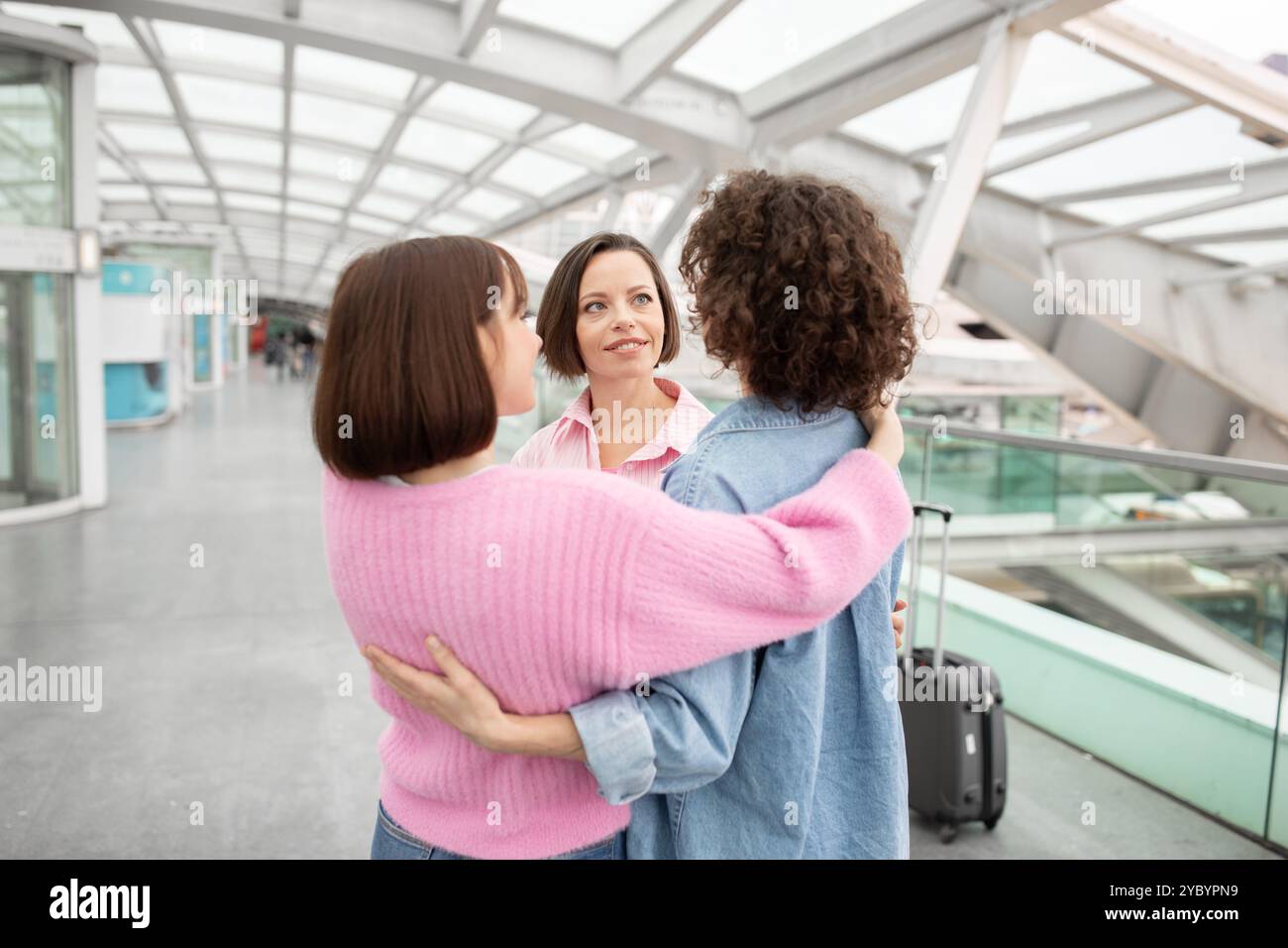Three friends embrace joyfully in a modern airport terminal during ...