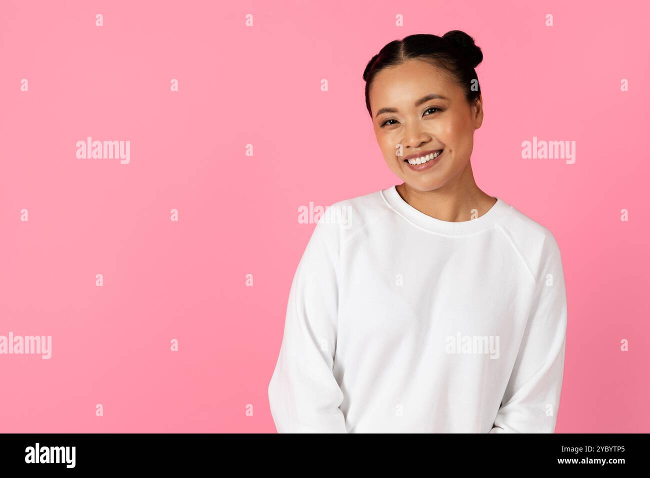 Young woman with a cheerful smile poses against a vibrant pink ...