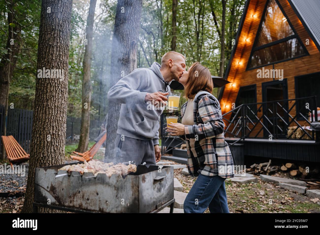 Romantic couple kissing while toasting with beer near a grill, enjoying ...