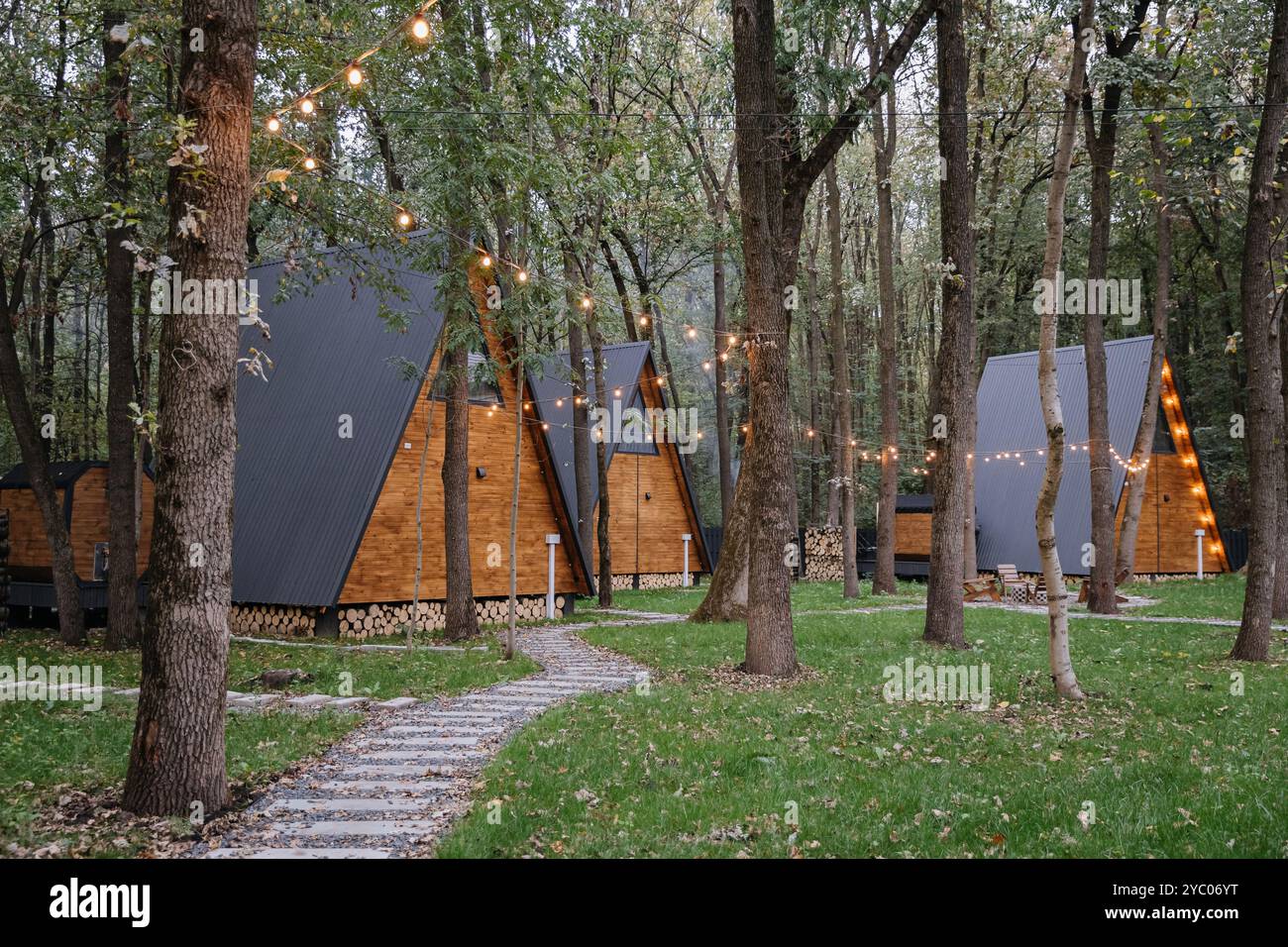 Modern A-frame cabins with glowing string lights in forest environment ...