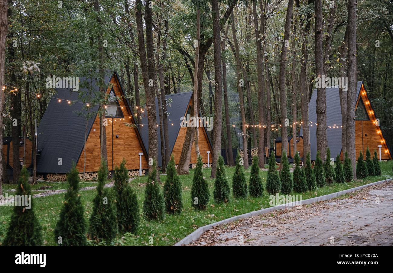 Cozy wooden A-frame cabins in forest with sunlight and outdoor seating ...