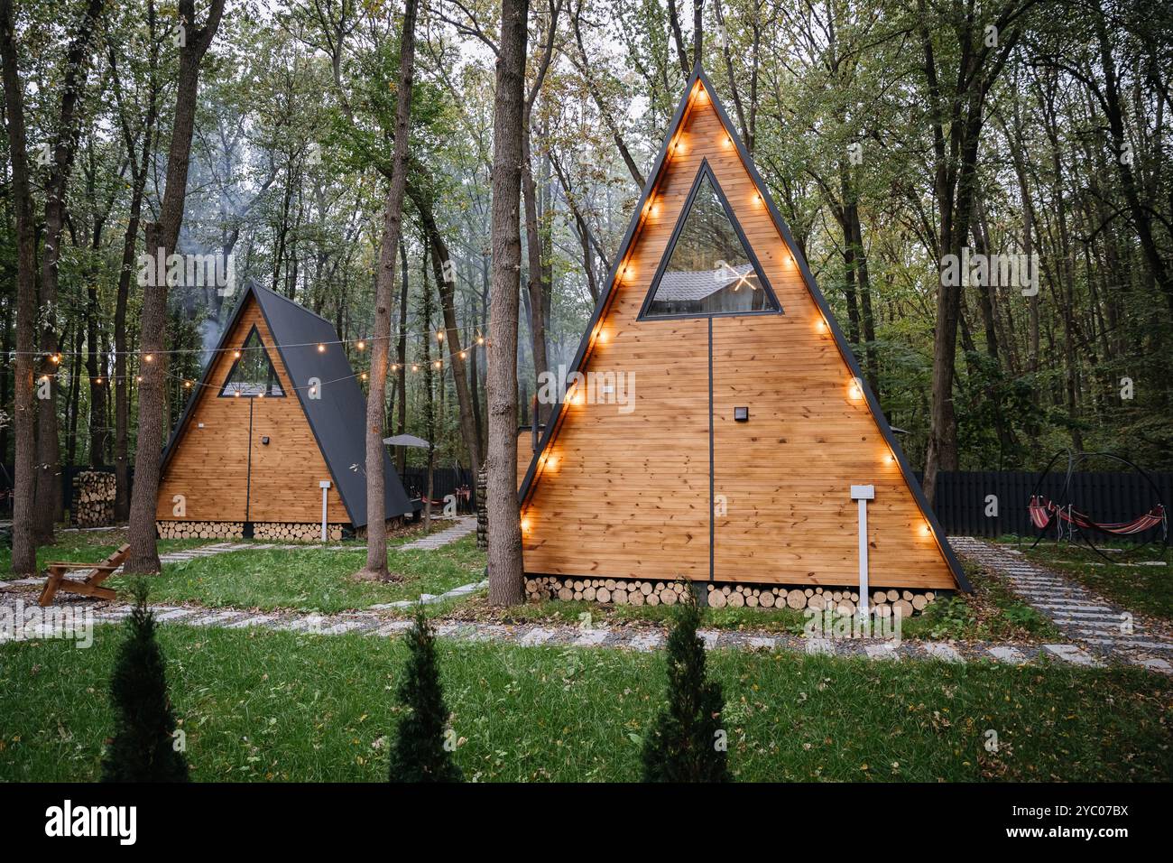 Modern A-frame cabins with glowing string lights in forest environment ...