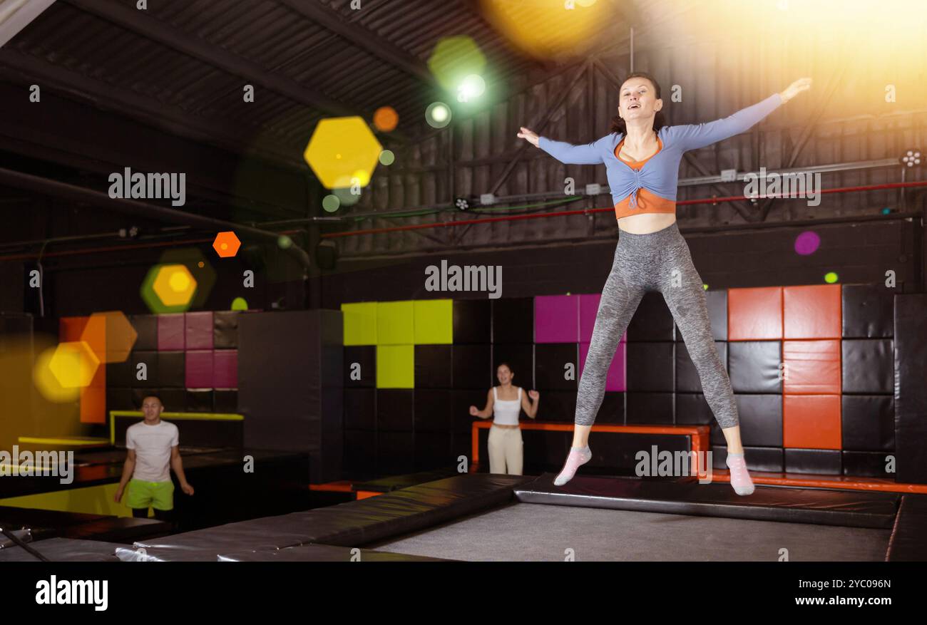 Excited woman enjoying jumping at well-equipped indoor trampoline arena ...