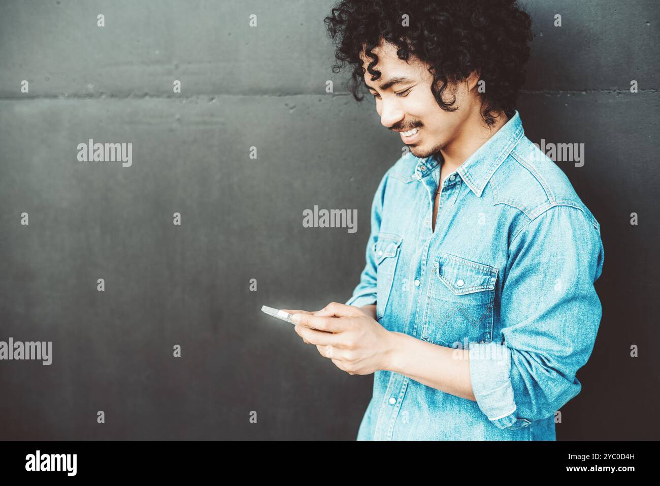 Young Filipino man with curly hair smiling while looking down at his ...