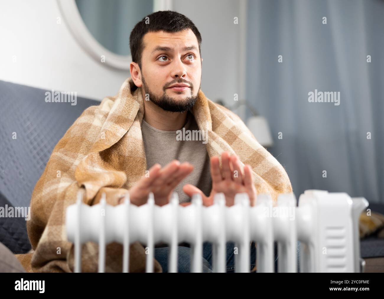 Man wrapped in cover warming hands at radiator in apartment Stock Photo ...