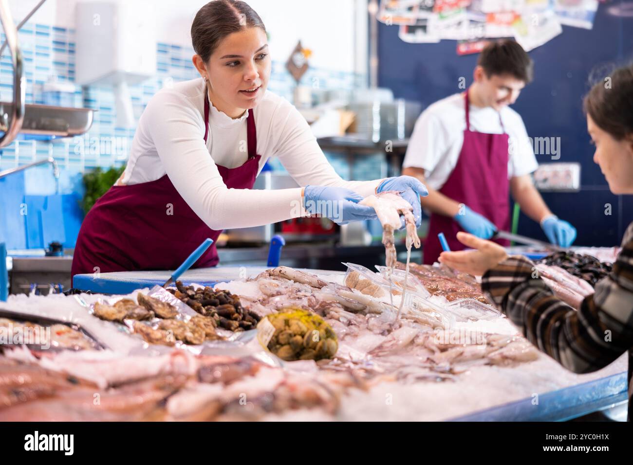 Portrait of female fishmonger showing fresh fish to woman behind ...
