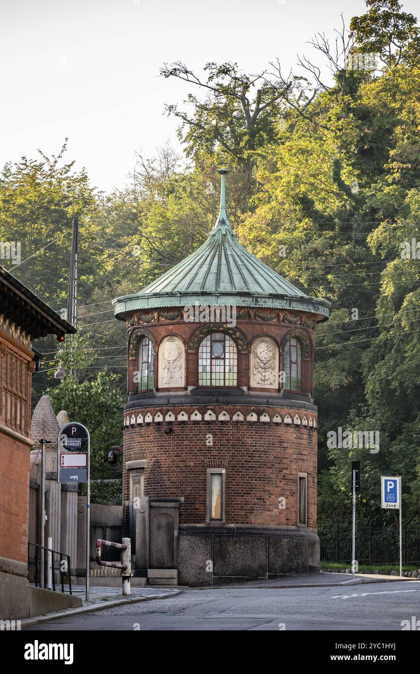 A small round brick tower with a green copper roof against a wooded ...