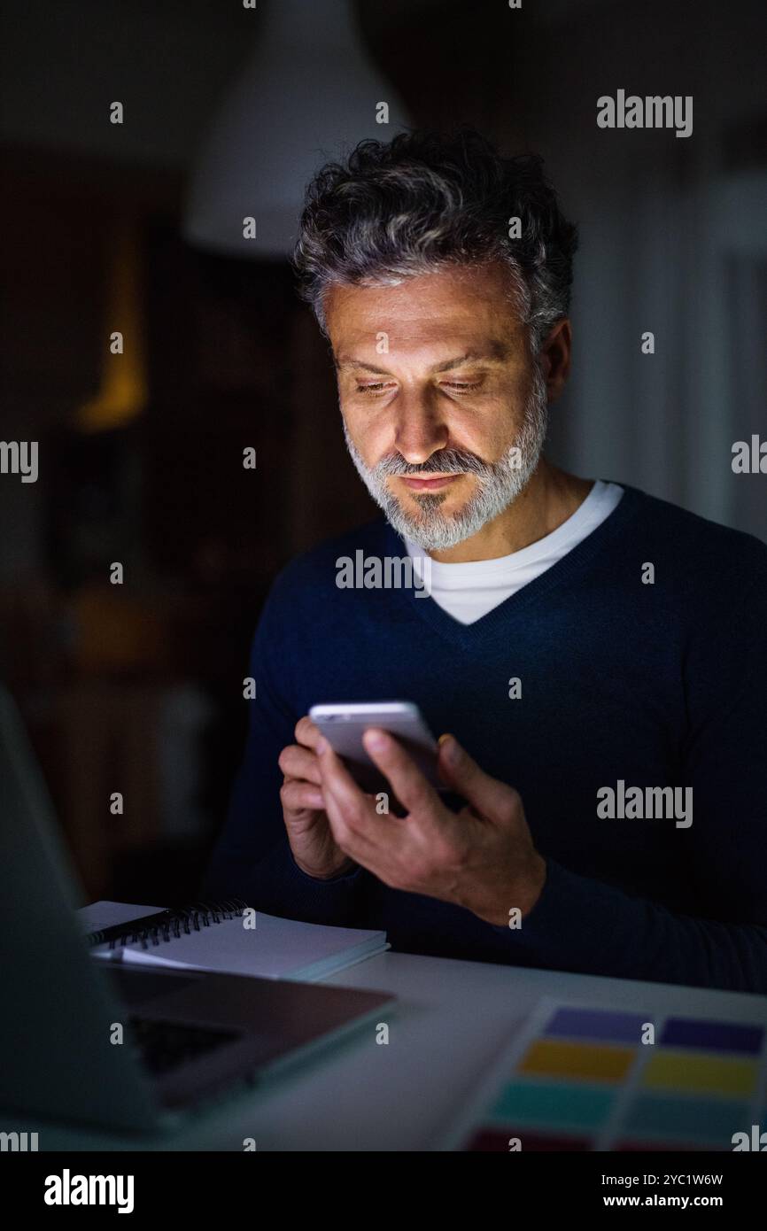 Handsome man working from home office at evening, holding smartphone ...
