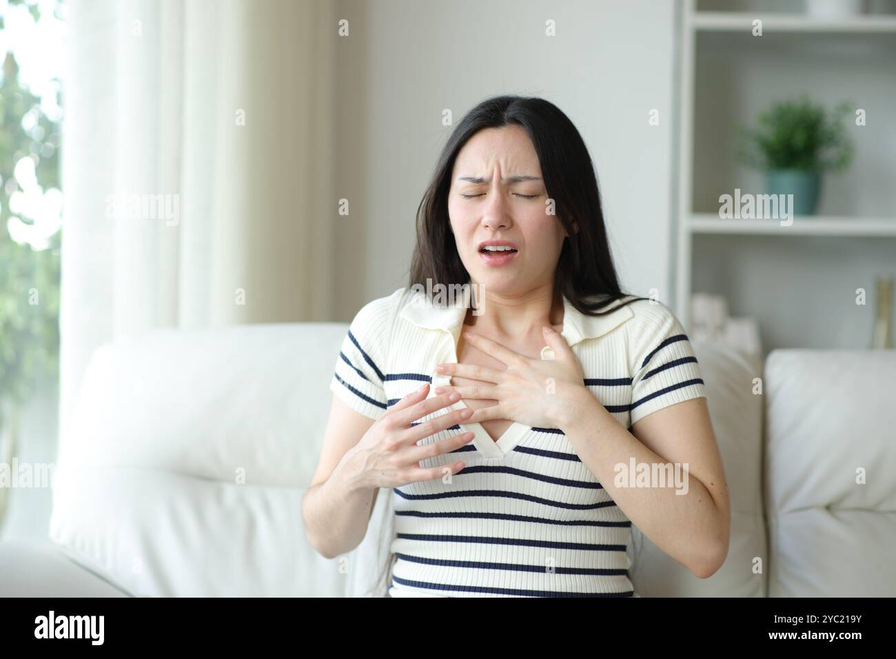 Asian woman chocking suffering asthma attack sitting on a couch at home ...