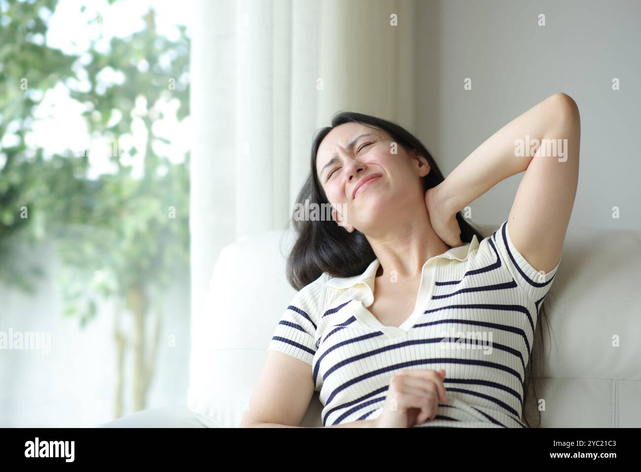 Stressed asian woman suffering neck ache sitting on uncomfortable couch ...