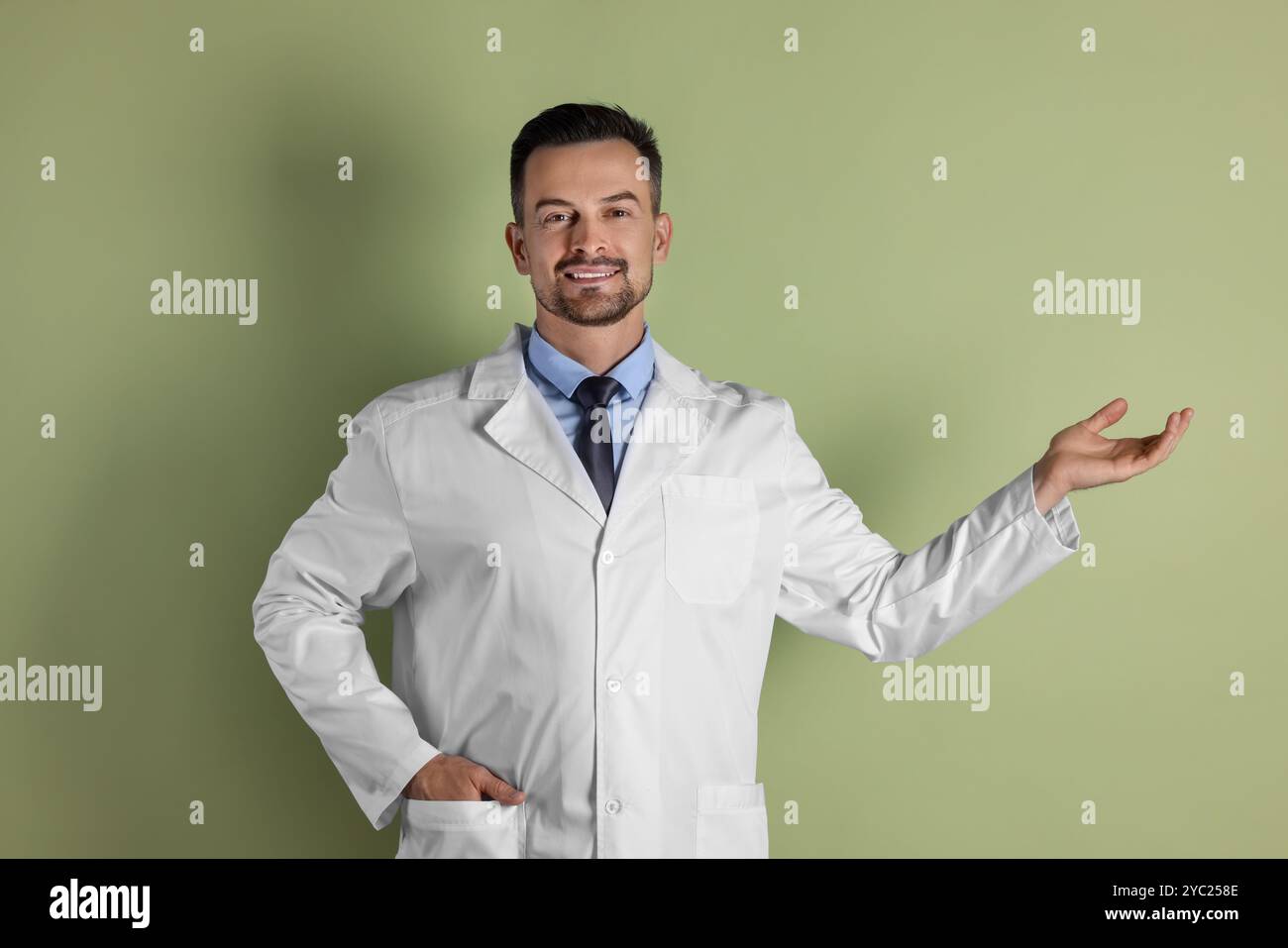 Smiling doctor pointing at something on olive background Stock Photo ...