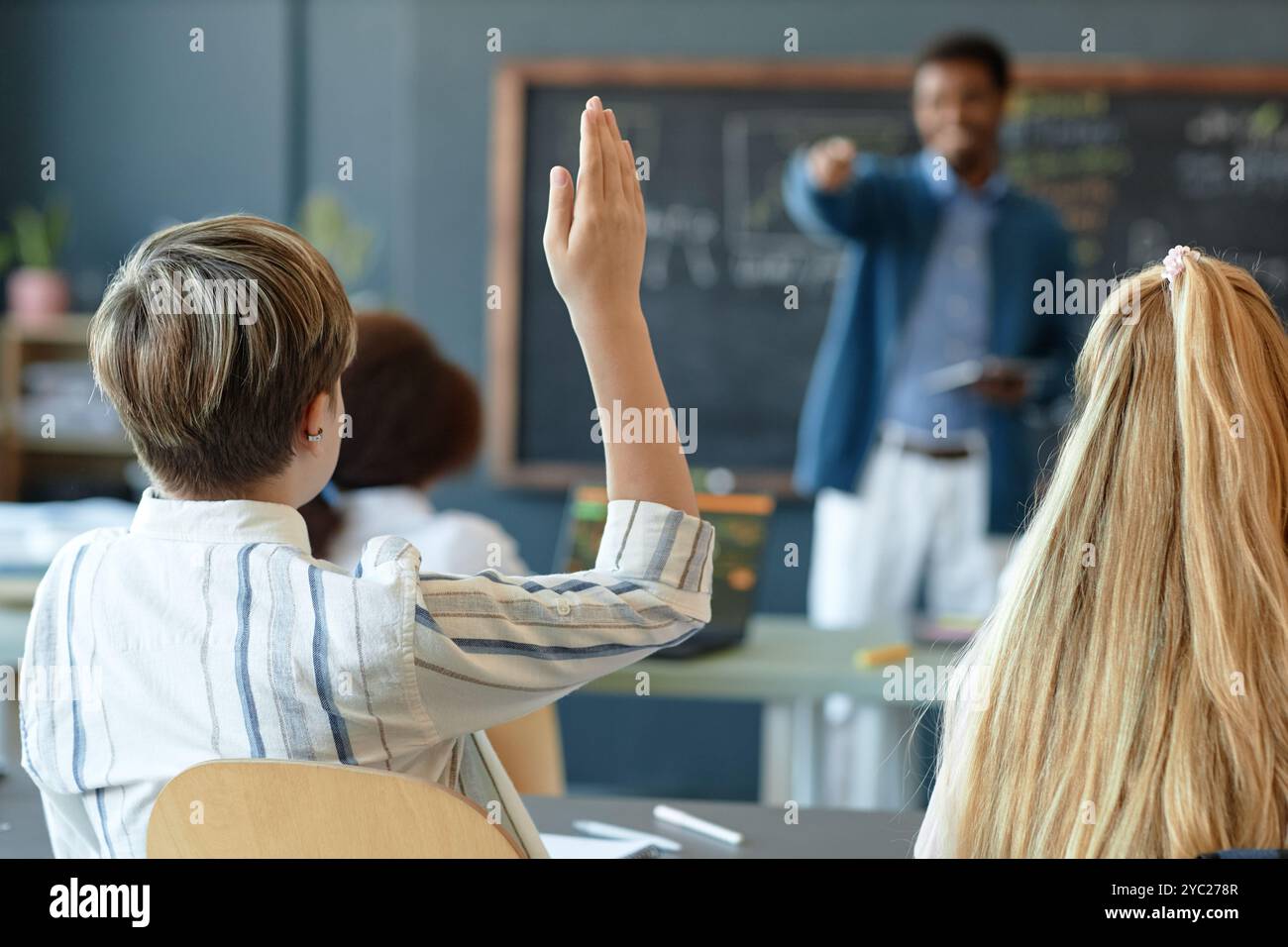 Back view of young boy raising hand in school class and answering ...