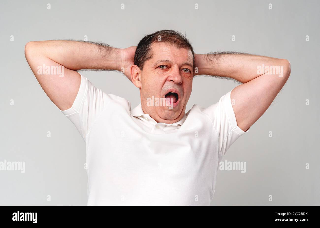 An older man stretching and yawning indoors while wearing a casual ...