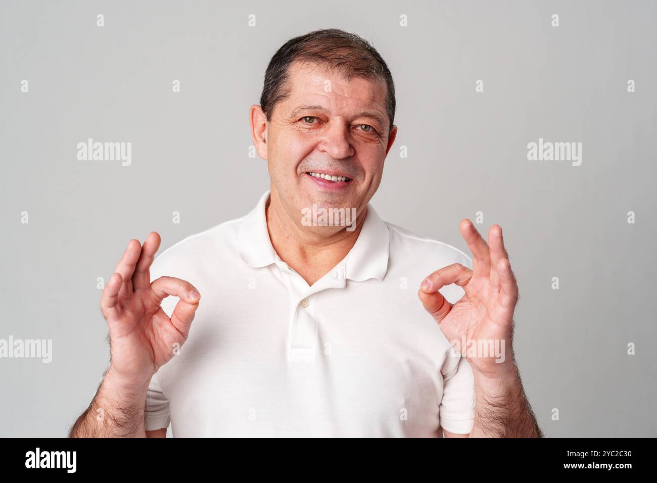 A man in a white shirt poses with a cheerful expression showing OK hand ...