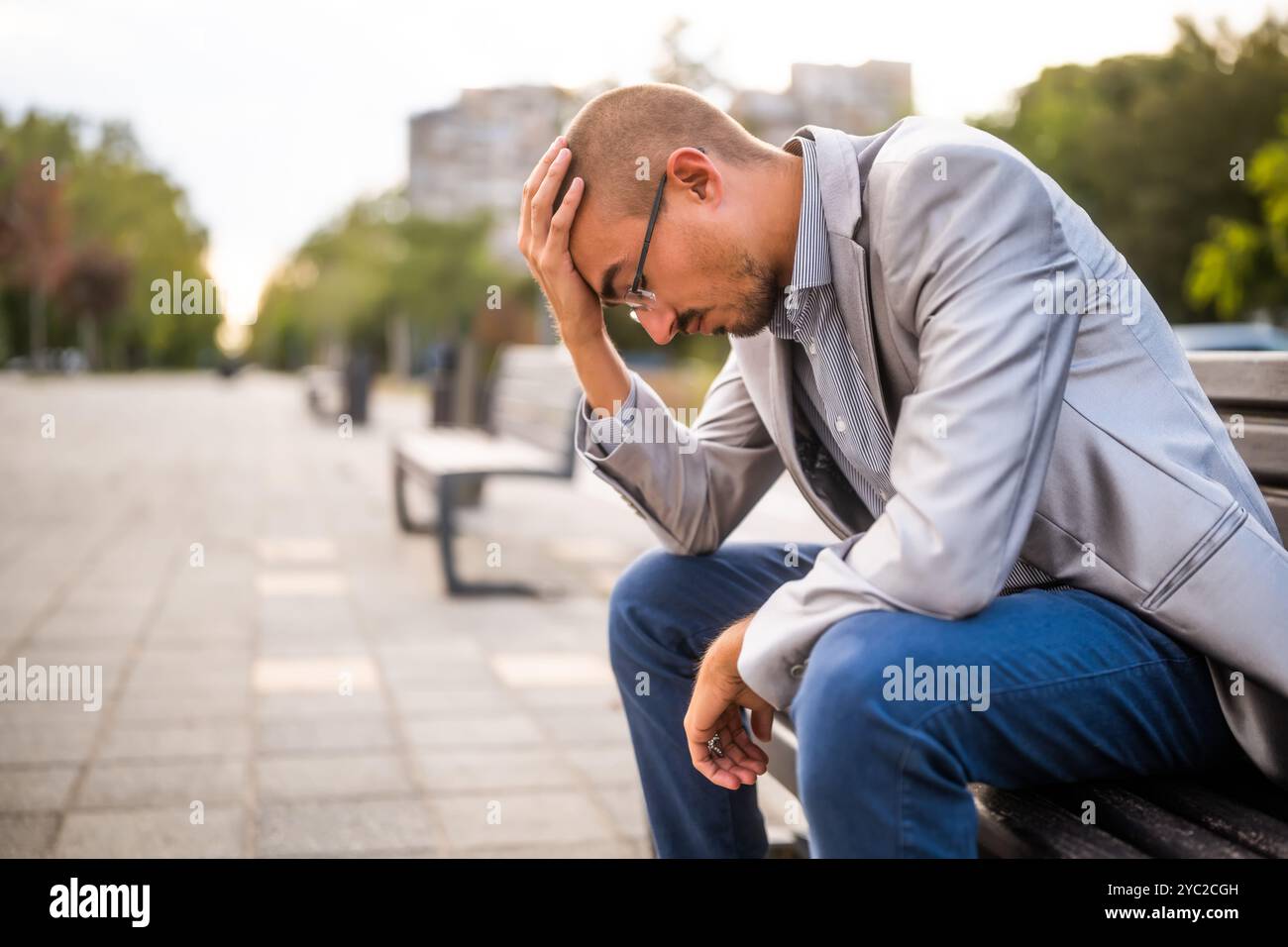 Portrait of overworked and depressed man. He is sitting on bench in the ...