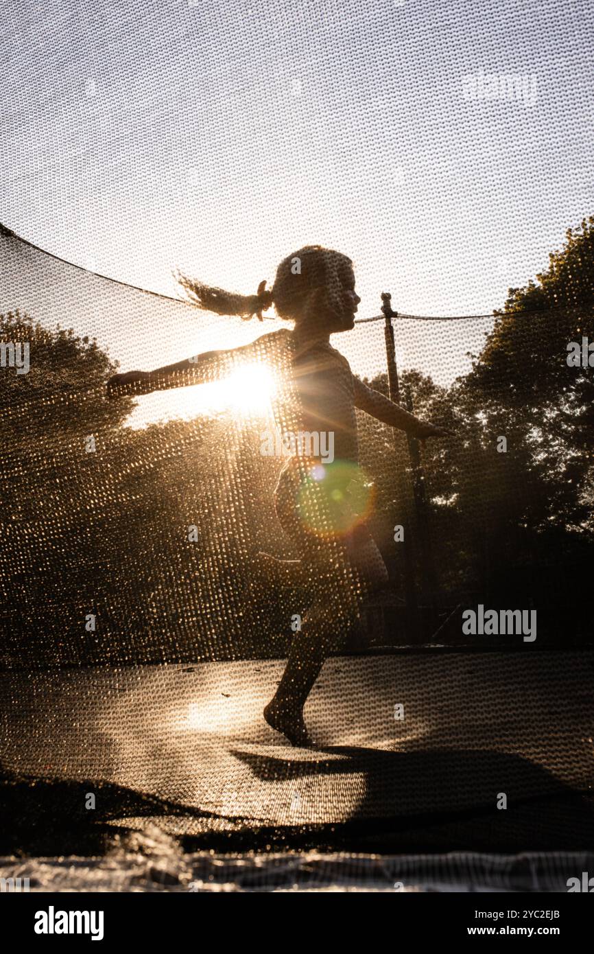 Carefree child twirling in golden light on trampoline Stock Photo - Alamy