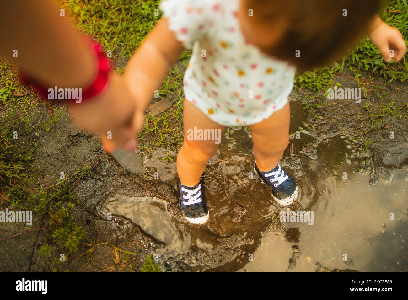 Toddler holding mothers hand while playing in mud puddle Stock Photo ...