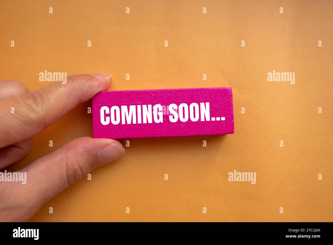 Coming soon message written on pink wooden block with orange background ...