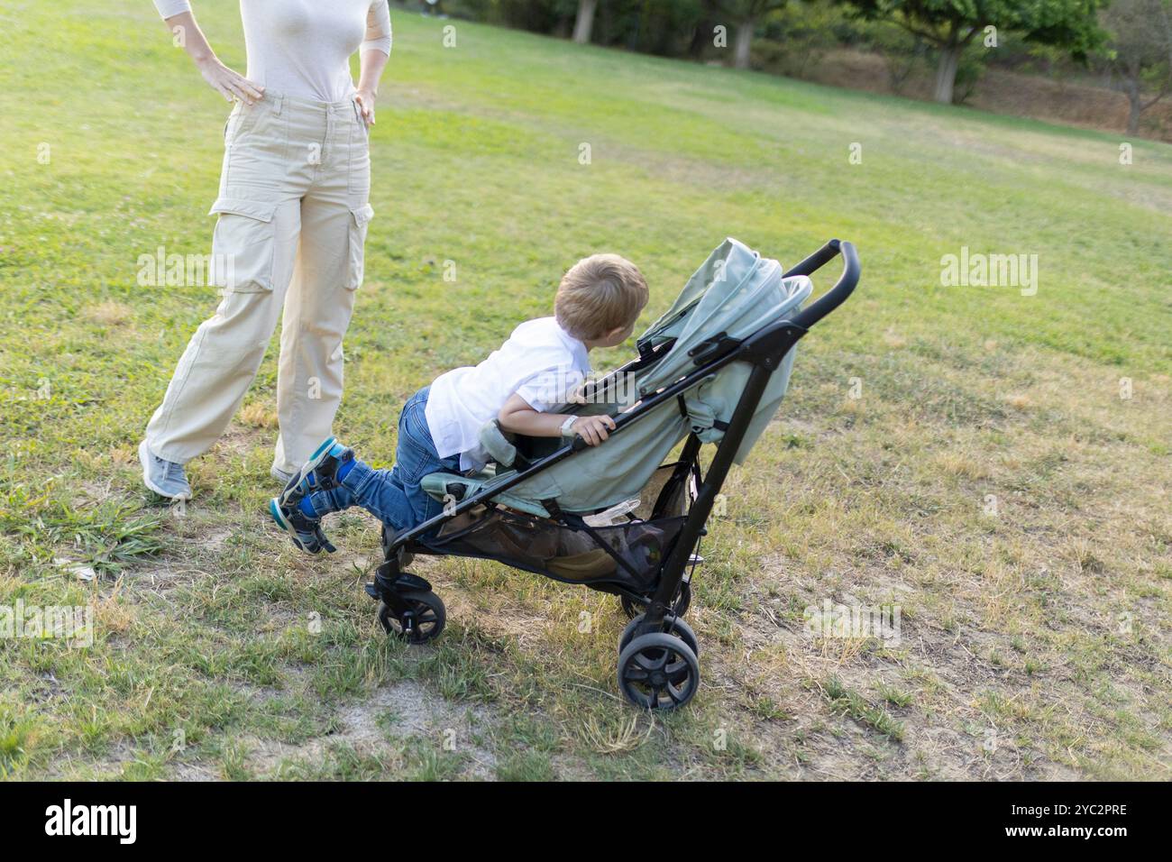 Little boy is pushing an empty stroller in the park while his mother ...