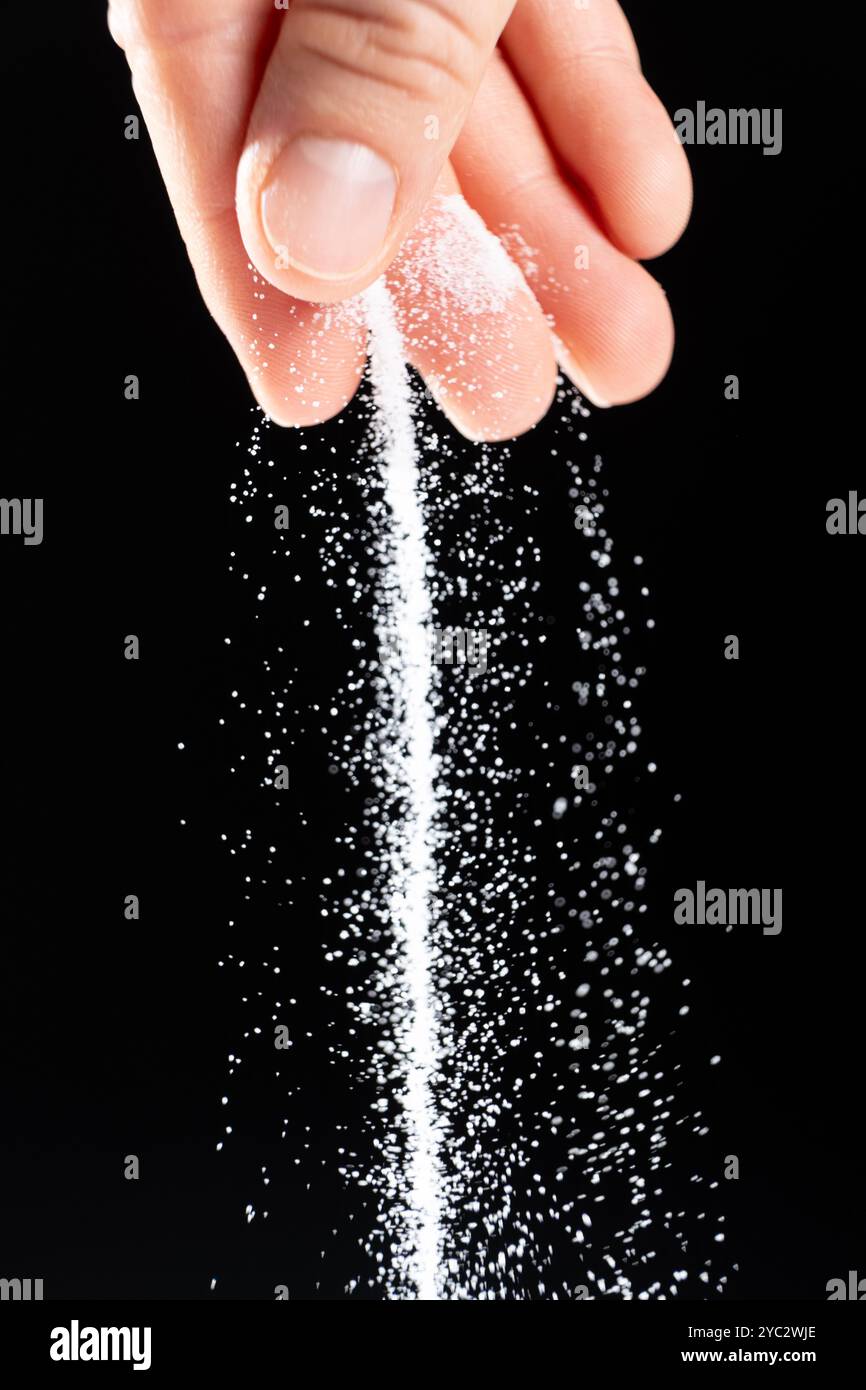 Hand pouring white stone salt finely ground, black background Stock ...