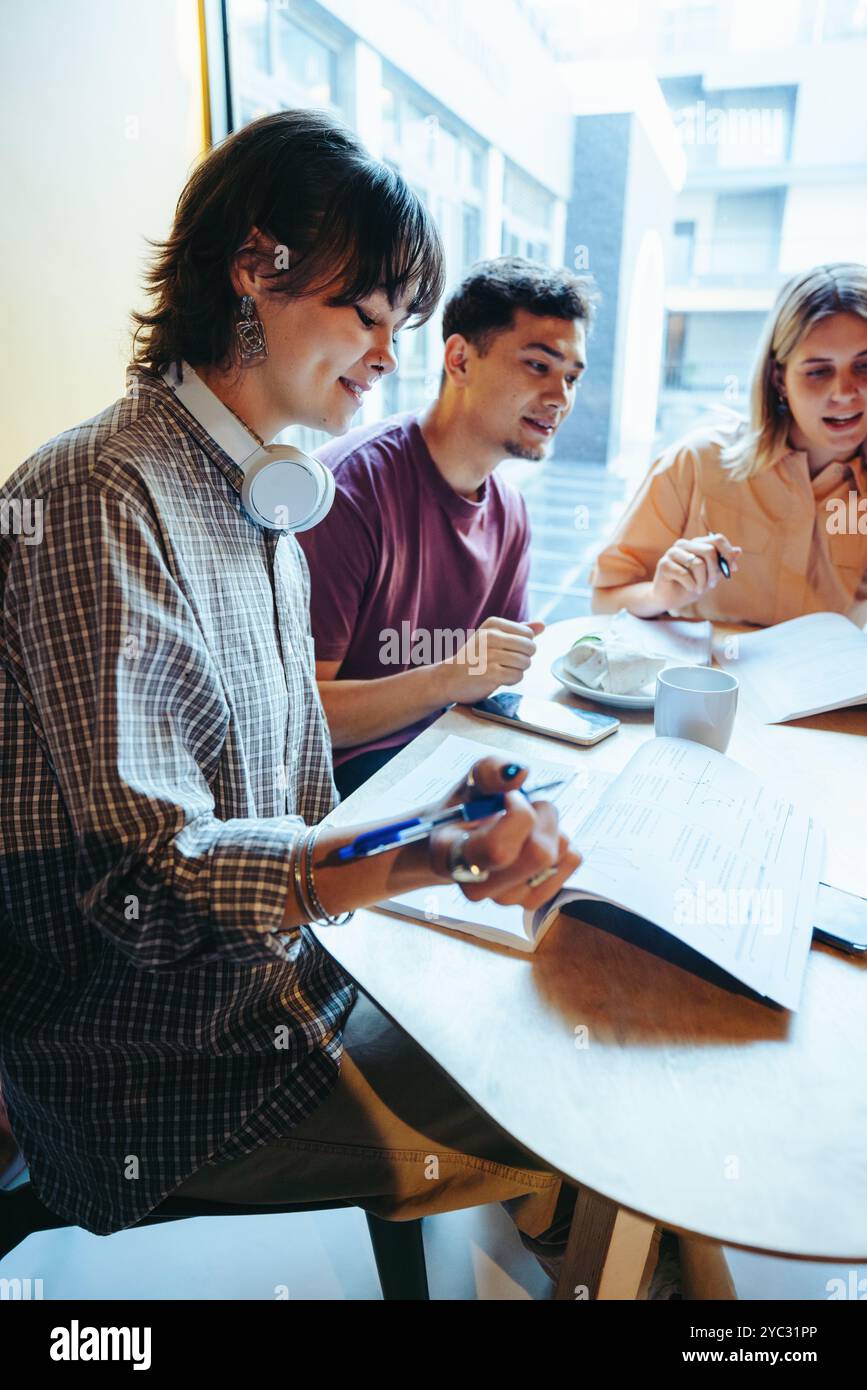 Young adults engaged in a university study session at a cafe, working ...