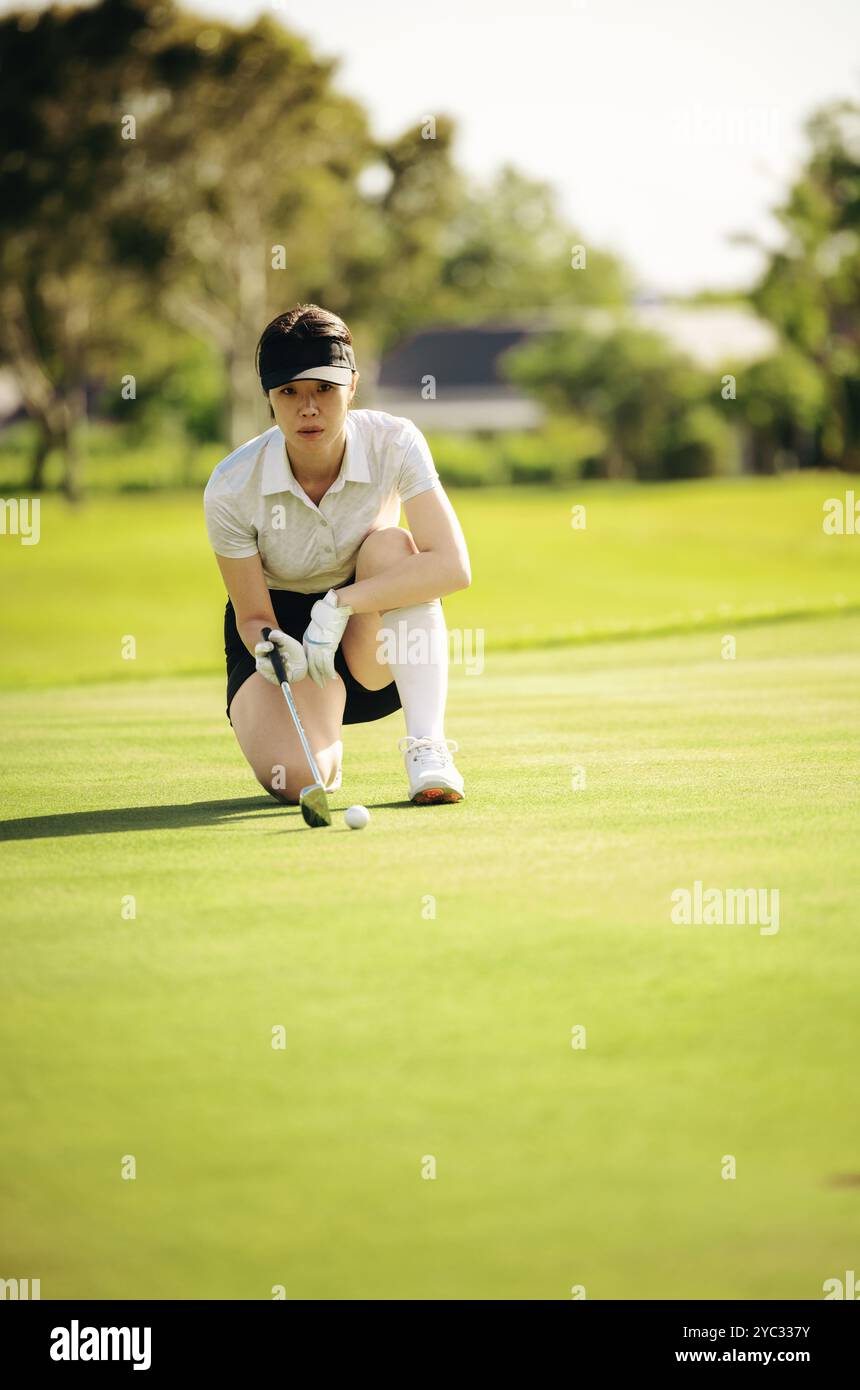 A focused woman golfer crouching on a golf course, ready to make a ...