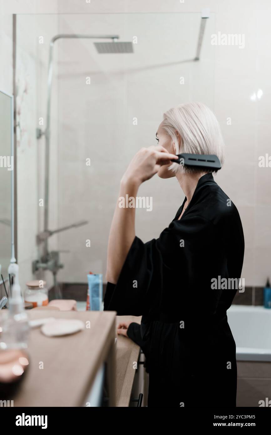 Woman brushing short hair in modern bathroom setting Stock Photo - Alamy