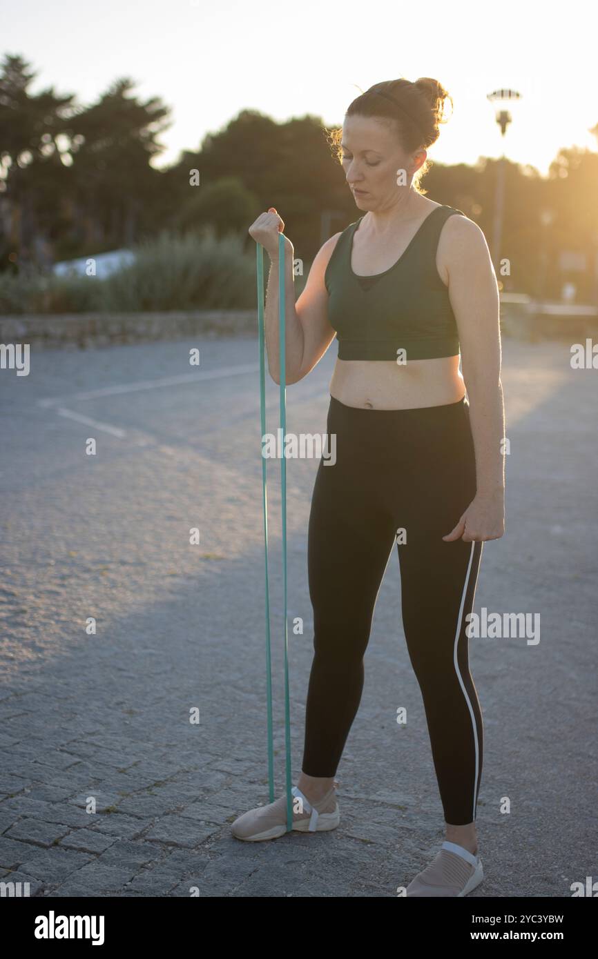 Athletic woman performing biceps curl with resistance band outdoors ...