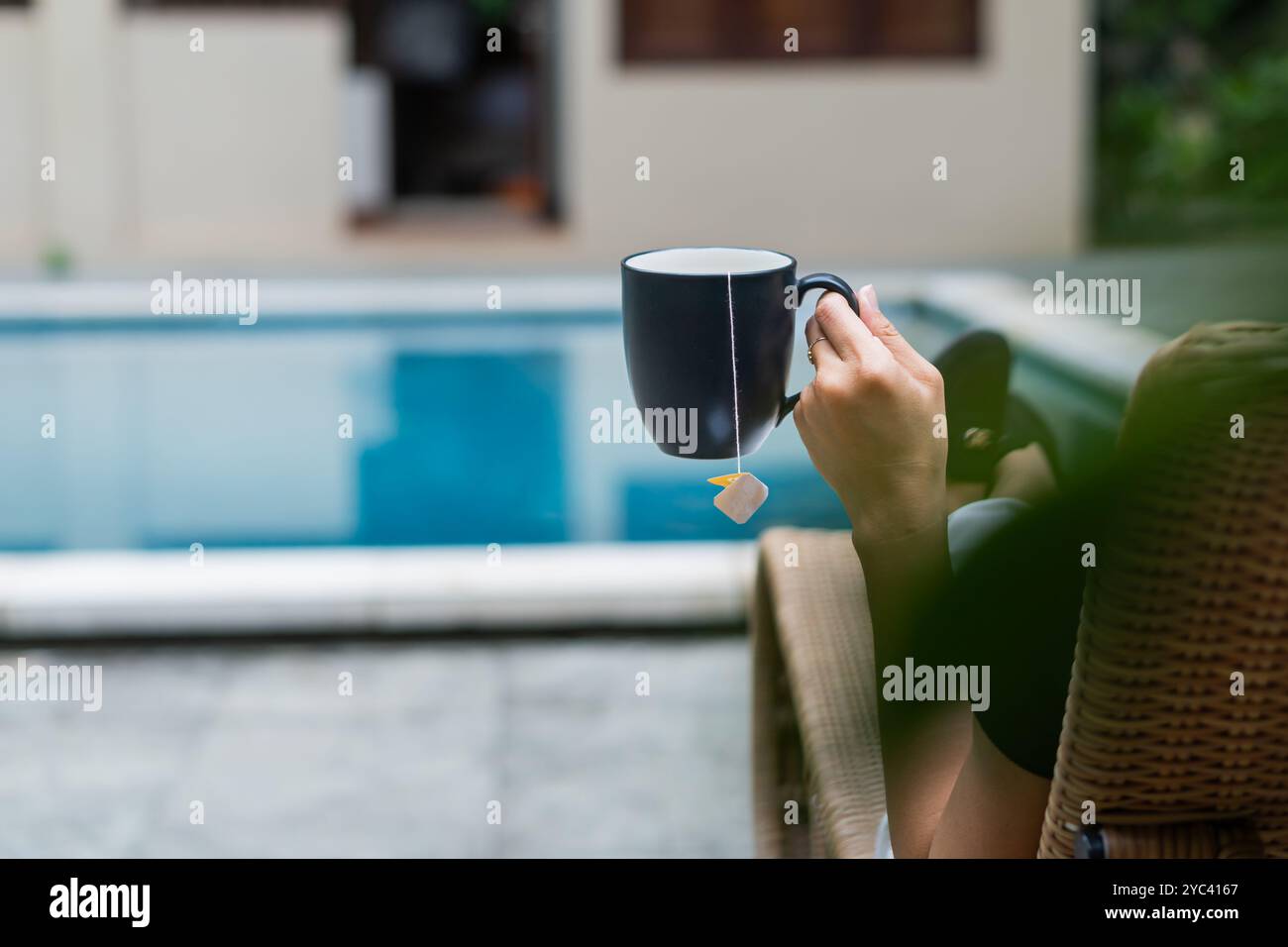 A person relaxing by a swimming pool, holding a cup of tea with a ...