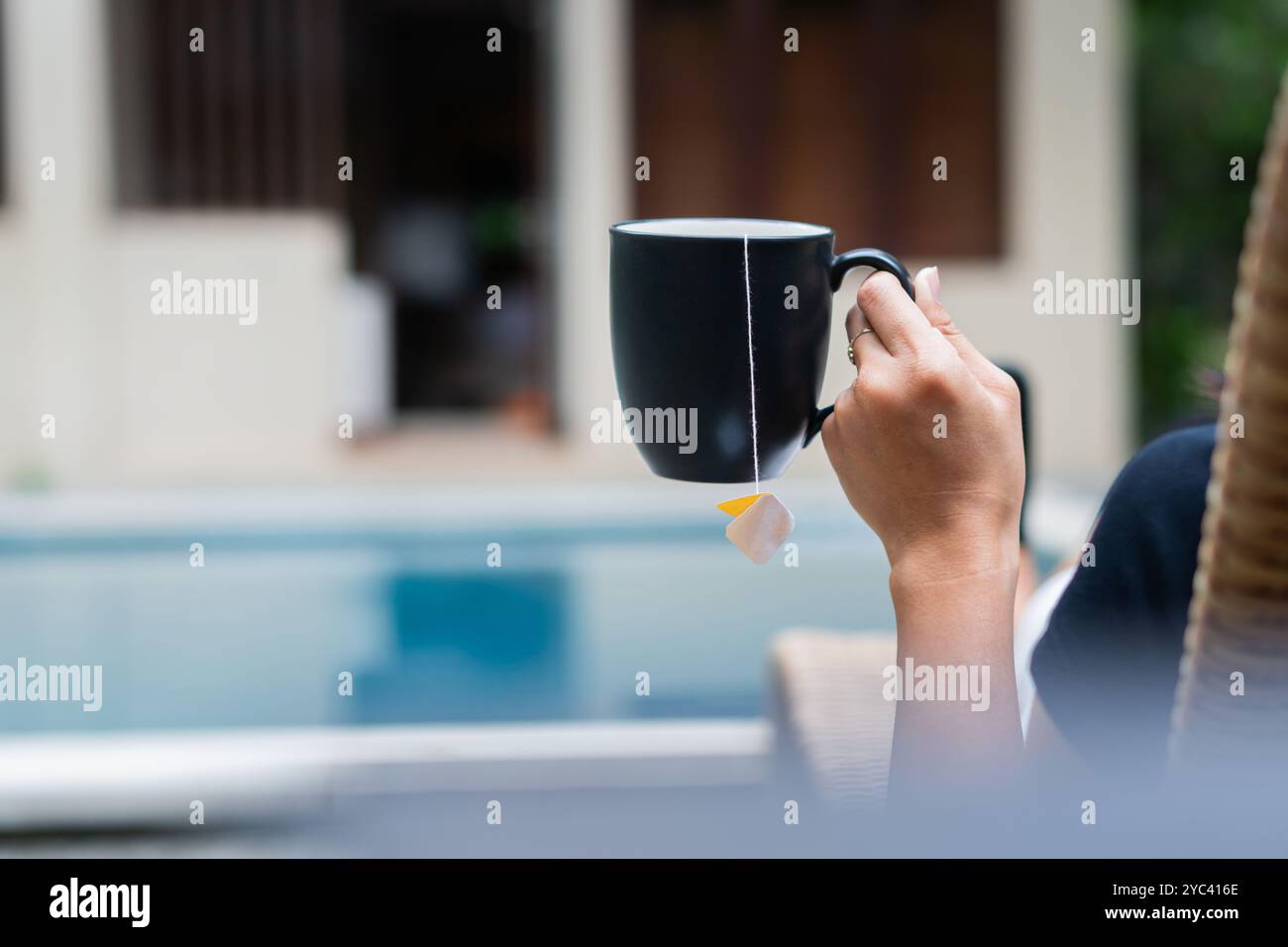A person relaxing by a swimming pool, holding a cup of tea with a ...