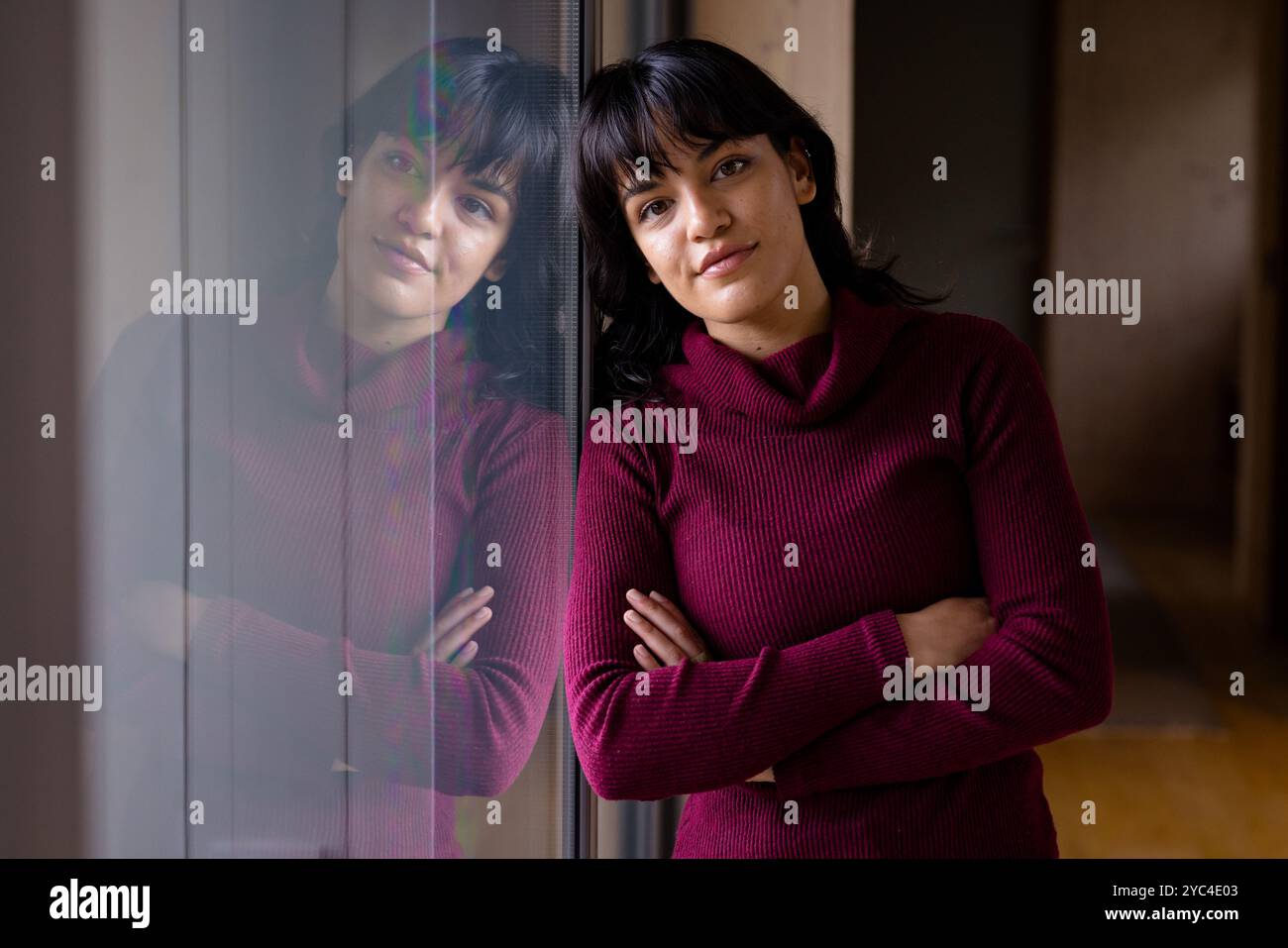 Woman in cozy sweater leaning against window, reflecting and smiling ...