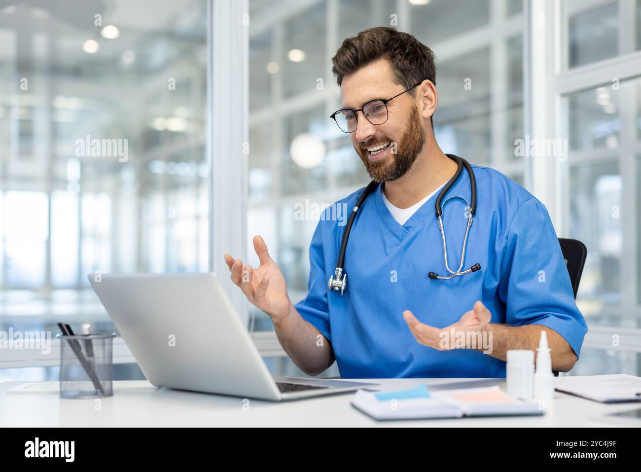 Smiling doctor wearing blue medical uniform conducts online ...