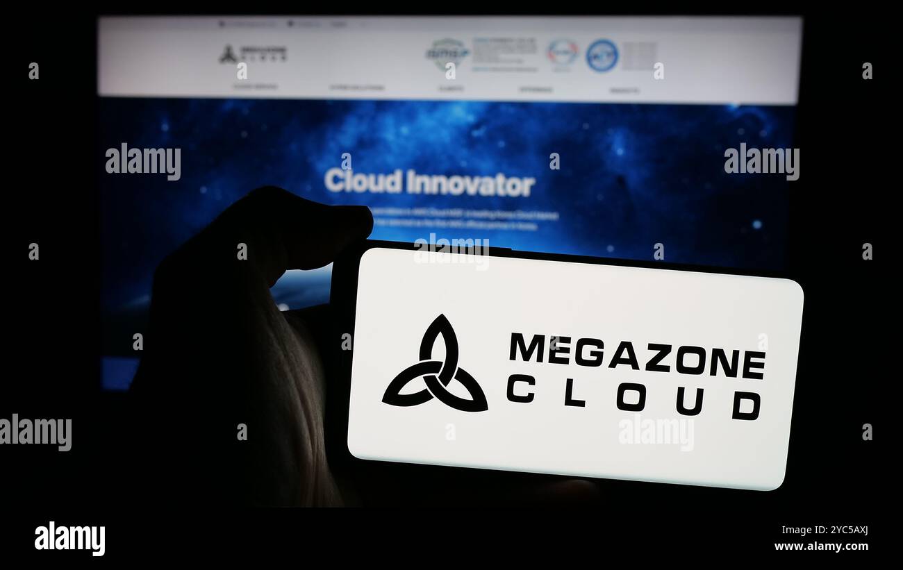 Person holding mobile phone with logo of South Korean company MegazoneCloud Corp. on screen in ...