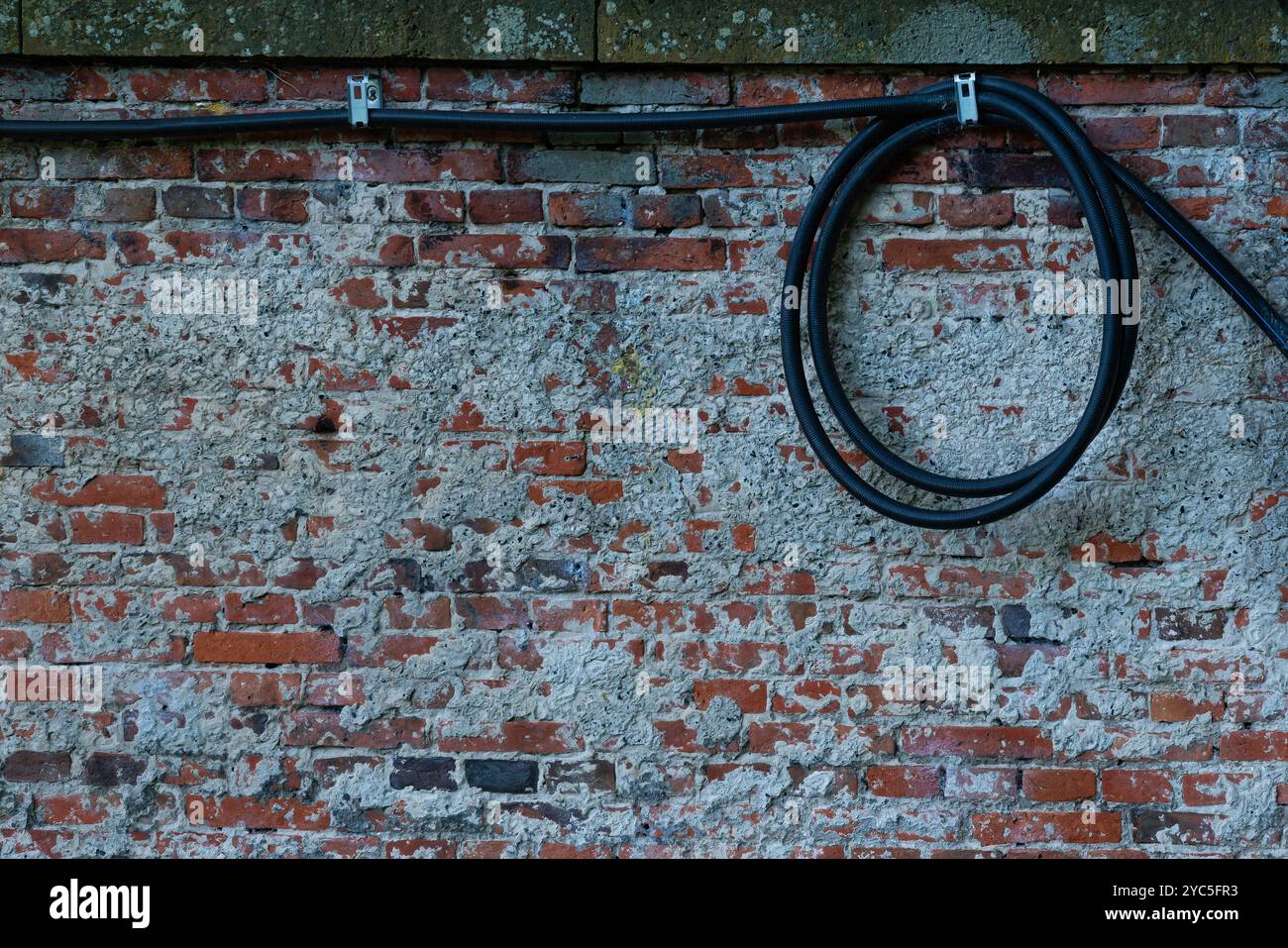 A black cable is neatly coiled against a textured, weathered brick wall ...