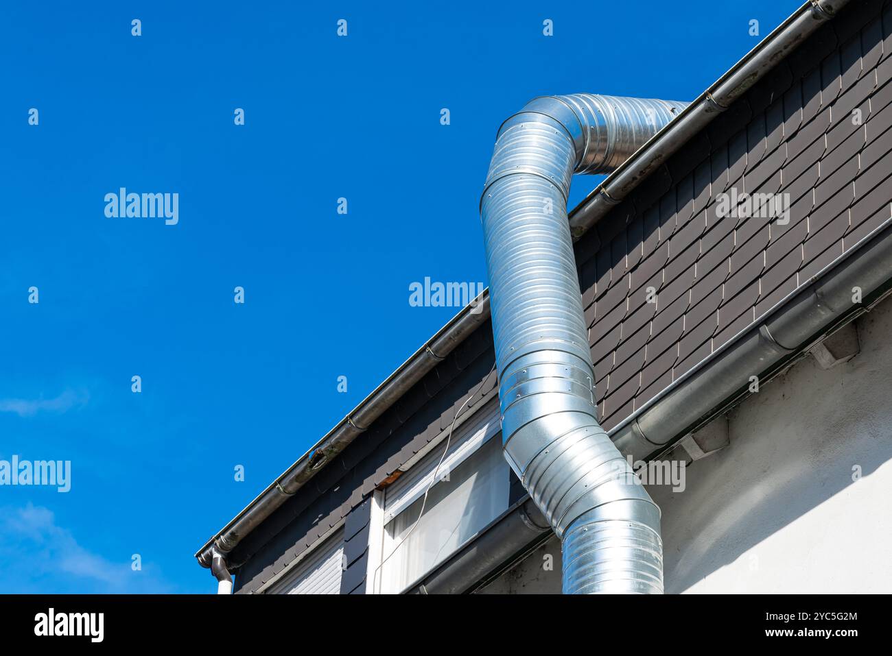 A shiny metal duct curves from the edge of a residential roof into the ...