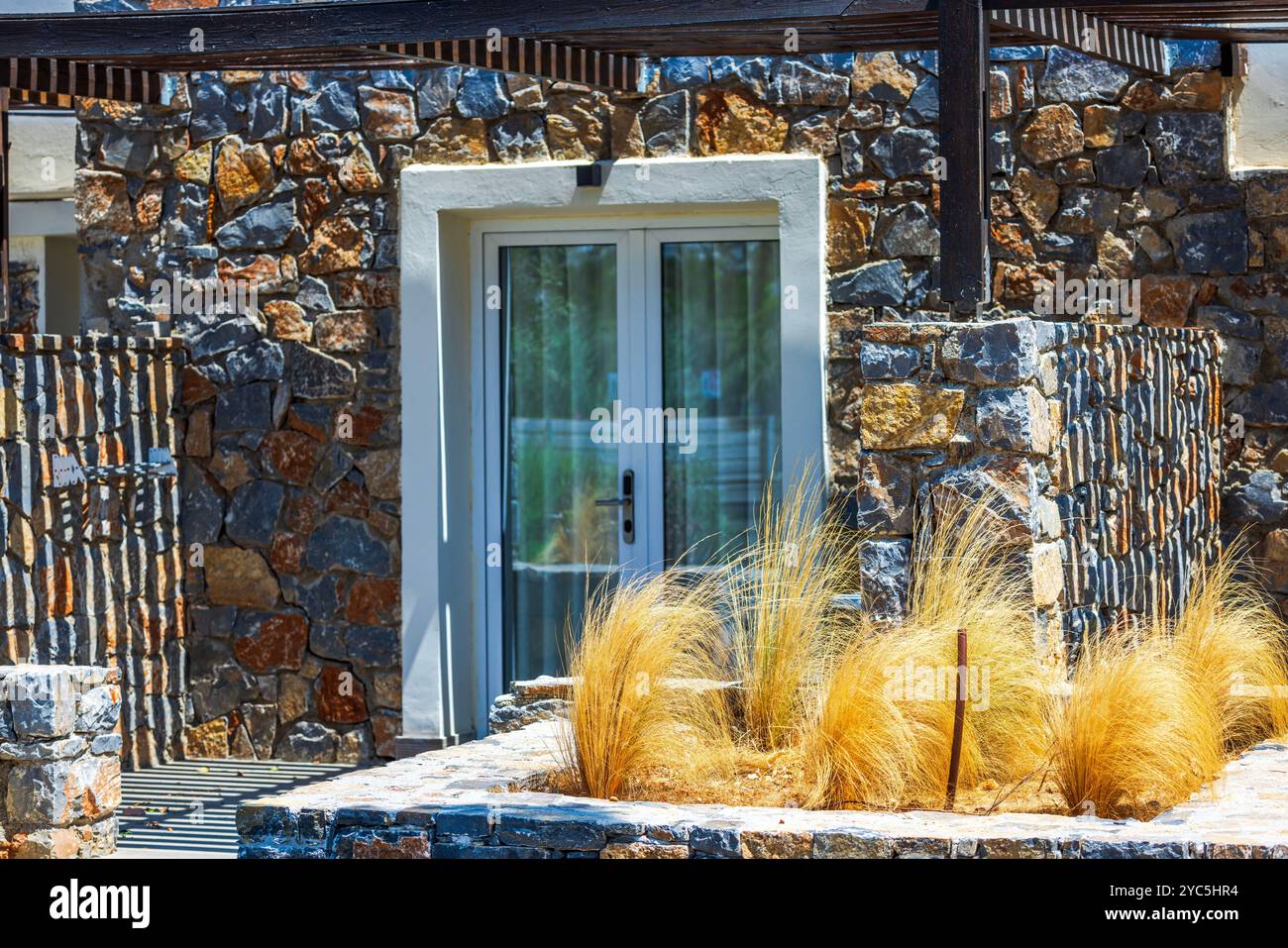 Stone facade of modern villa with tall yellow grass in foreground under ...