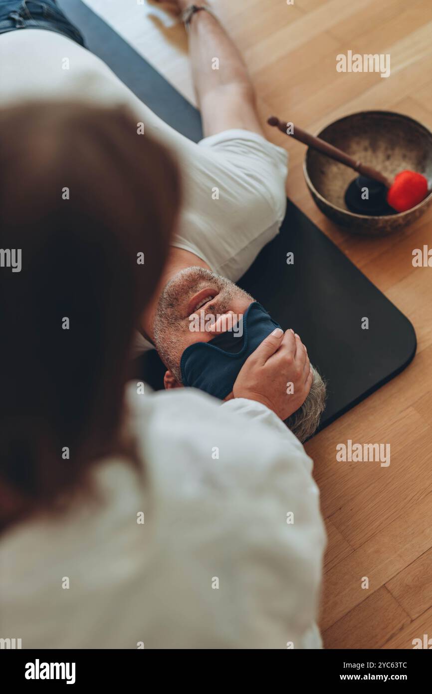 A man lying on a mat with a blindfold, practicing breathing exercises ...