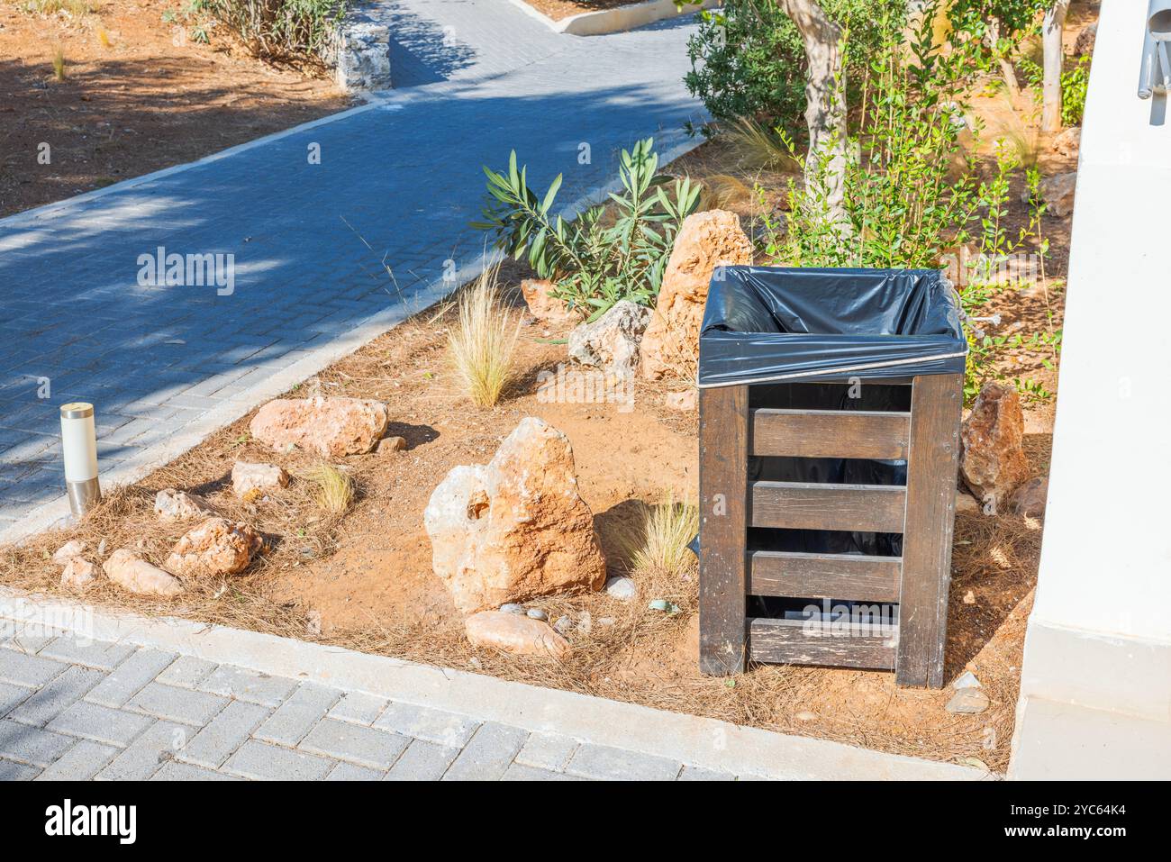 Outdoor trash bin with black liner, surrounded by rocks and plants ...