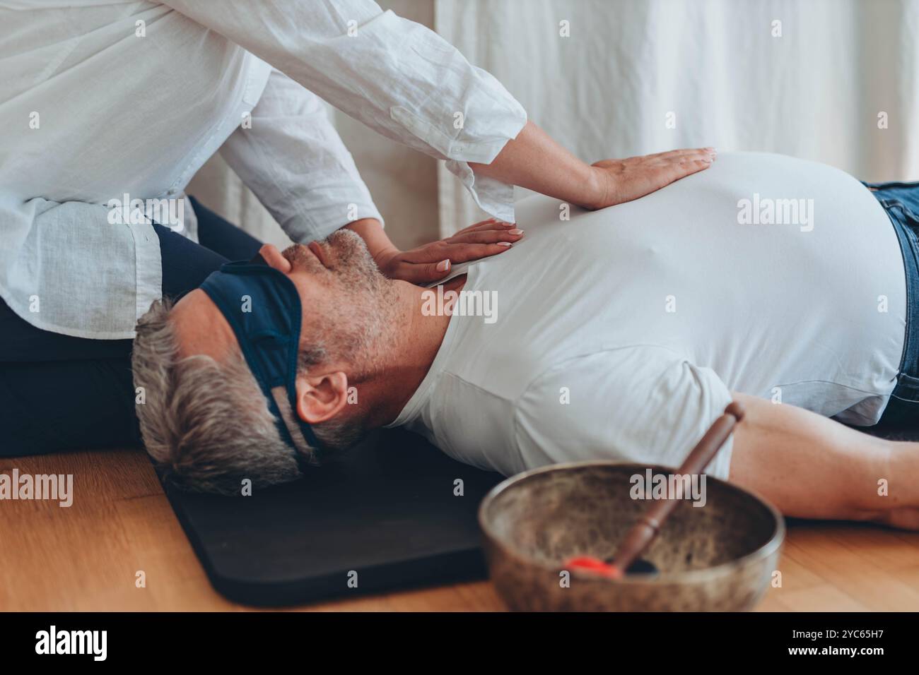 A man lying on a mat with a blindfold, practicing breathing exercises ...