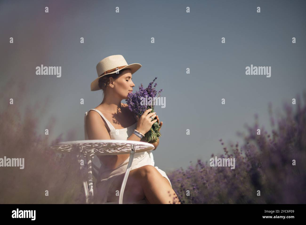 A woman is sitting in a field of lavender flowers and wearing a straw ...