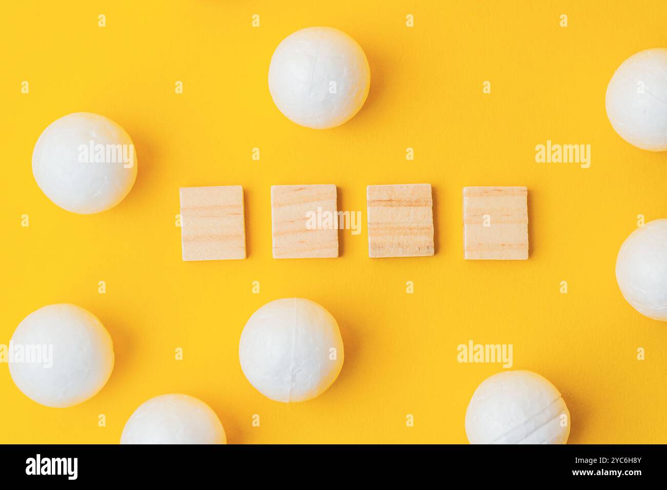 Wooden cubes and white spheres arranged on a bright yellow background ...