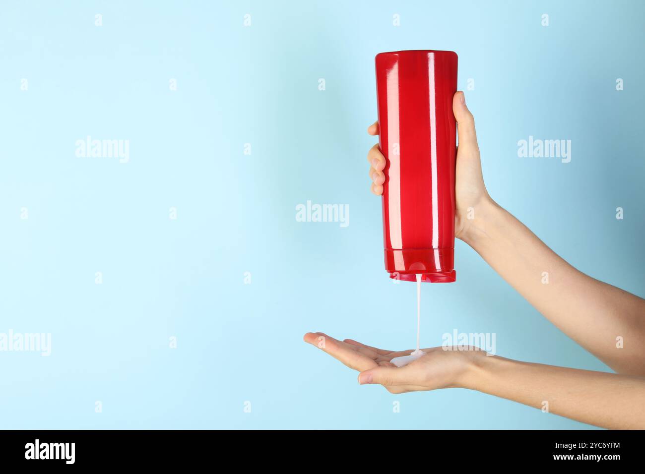 Woman pouring shampoo onto hand on light blue background, closeup ...