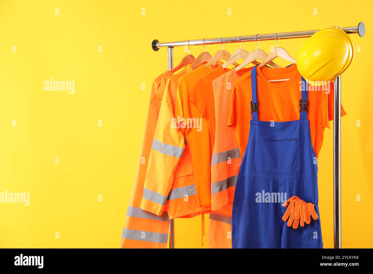Workers' uniforms on clothing rack against yellow background. Space for ...