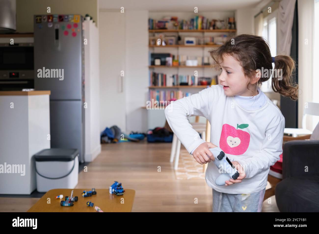 A little girl plays at home with a game console controller during ...