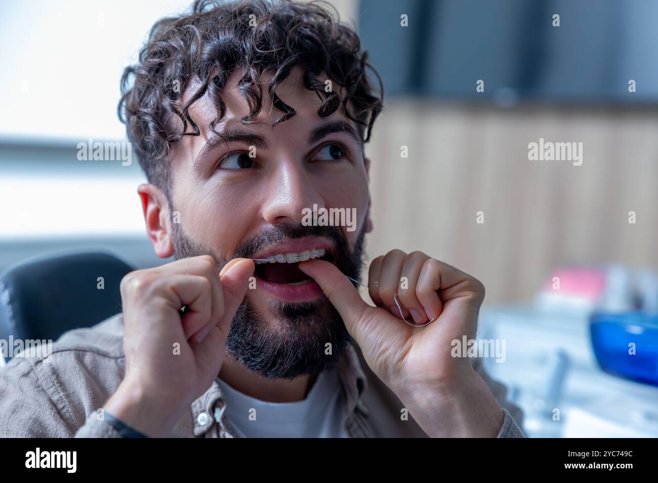 Bearded man carefully flossing his teeth and braces doing hygienic ...