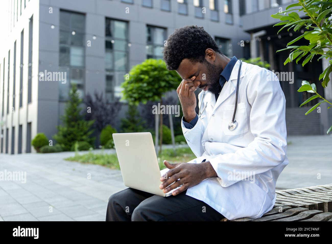 Tired doctor wearing his uniform at hospital using his laptop for ...